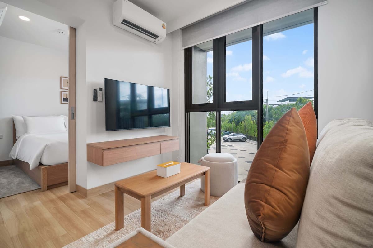 Quarto de hotel moderno com cama, televisão na parede, mesa de madeira e uma janela grande com vista para o exterior.