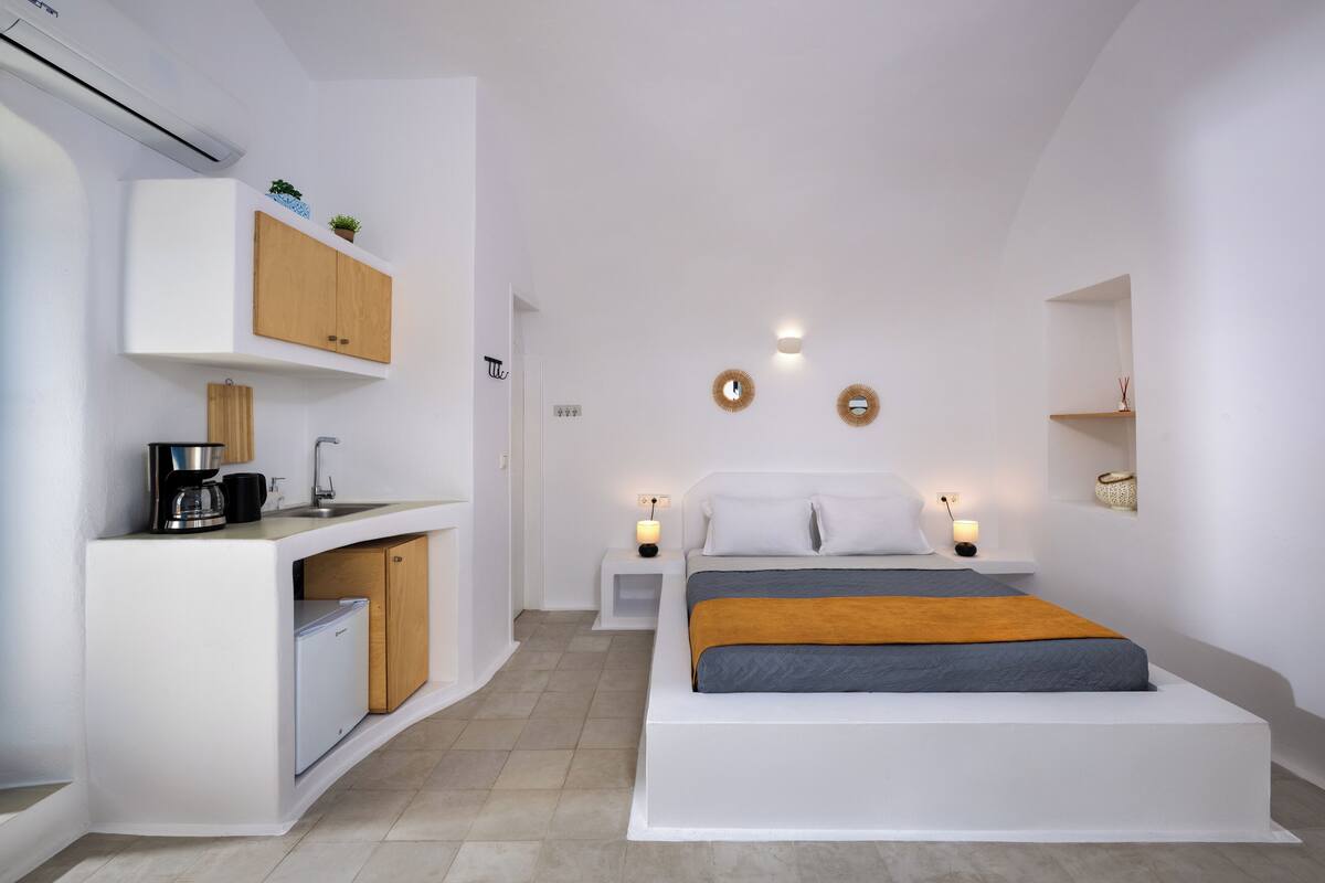 Quarto moderno com cama, mesas de cabeceira, guarda-roupa embutido, pequena cozinha e prateleira na parede.
