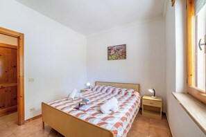 Um quarto com uma cama, mesa de cabeceira, janela e porta.