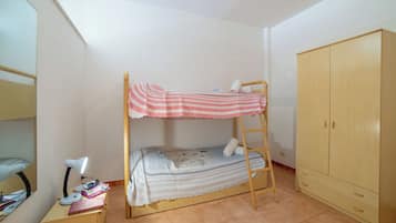 Uma cama beliche com um cobertor listrado, uma escrivaninha com abajur e um guarda-roupa.