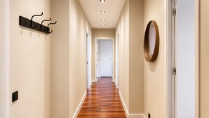 Um corredor com piso de madeira, um porta-roupas, iluminação embutida e um espelho redondo na parede.