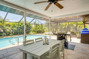 Uma área externa coberta com piscina, mesa e cadeiras, ventilador de teto e churrasqueira.