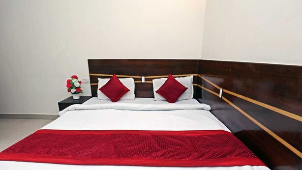 Cama bem arrumada com manta vermelha, almofadas brancas e cabeceira de madeira.