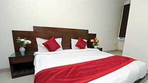 Quarto de hotel com cama, mesa de cabeceira, um vaso com flores e espelho.