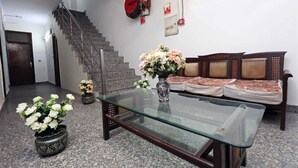 Uma escadaria, uma mesa com tampo de vidro, um sofá e dois vasos com flores.