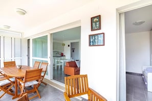 Uma sala de jantar com mesa e cadeiras de madeira, cozinha ao fundo e porta de vidro deslizante que dá para uma área externa.