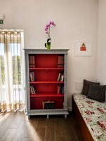 Um quarto com uma estante vermelha, uma cama com colcha florida e um vaso de planta verde na estante.