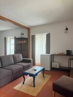 Uma sala de estar com sofá, mesa de centro, uma mesinha com chaleira e geladeira.