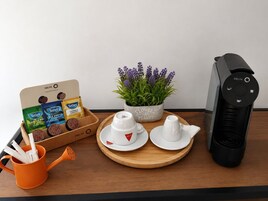Uma cafeteira, uma bandeja com bule e chávenas, uma caixa de saquinhos de Tetley, um copo com canudos e uma planta em vaso sobre uma mesa de madeira.