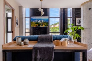 Uma sala de estar moderna com um sofá, uma mesa de centro e uma janela grande com vista para um horizonte urbano.