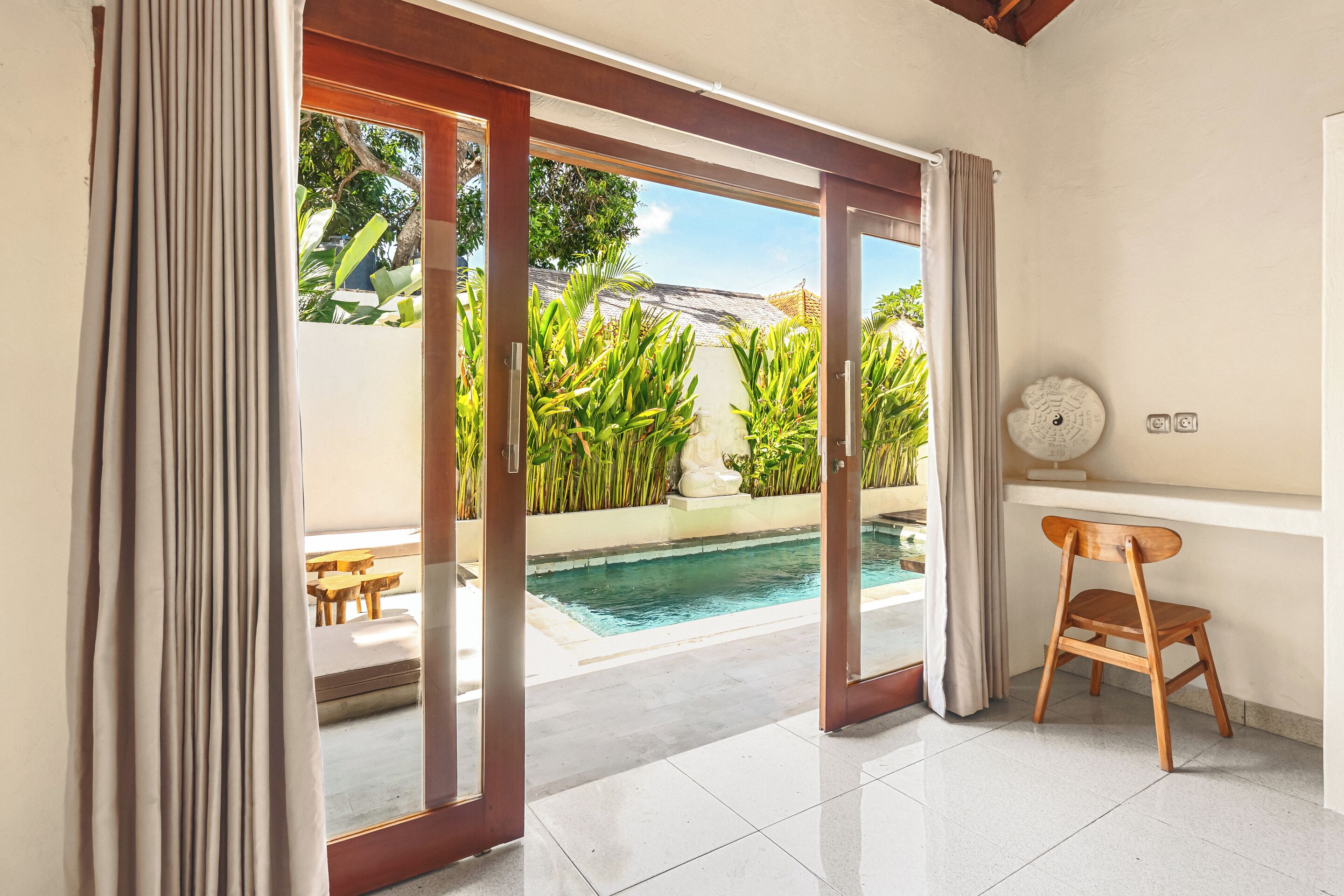 Quarto com porta de vidro deslizante que dá para uma área de piscina, uma cadeira de madeira e uma mesa pequena.