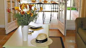 Quarto com uma mesa de jantar, cadeiras, um vaso de flores, um chapéu e uma janela com vista para o verde.