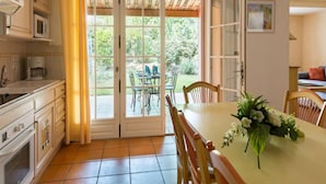 Uma cozinha com área de refeições, uma mesa com cadeiras e vista para um pátio exterior através de portas de vidro.