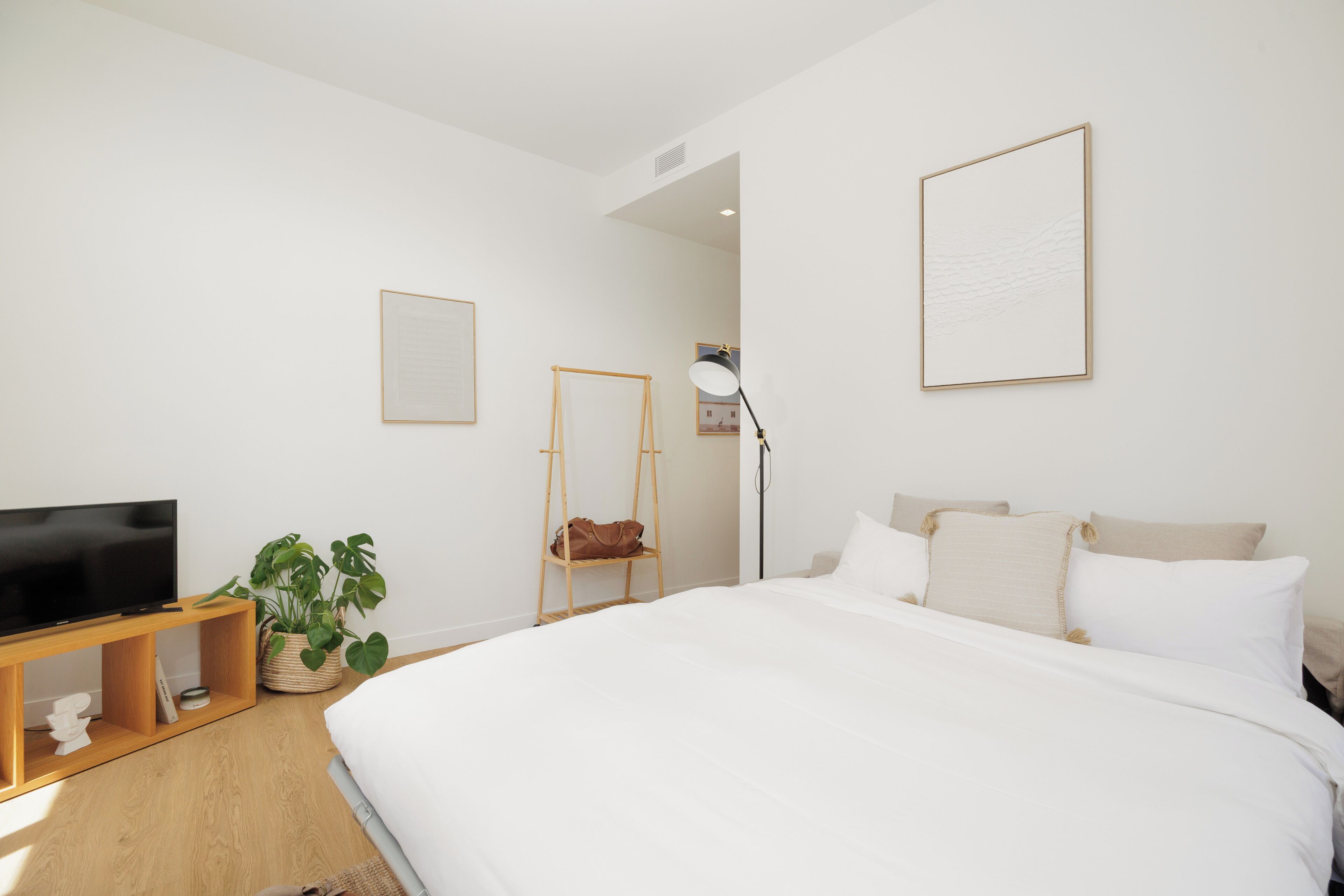 Quarto moderno com cama, televisão, planta e escrivaninha.