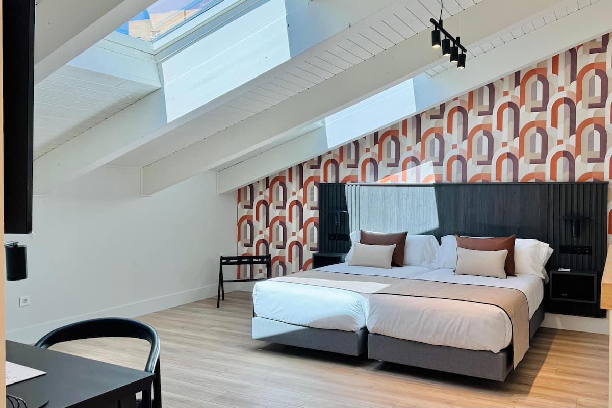 Quarto moderno com claraboia, cama com várias almofadas, mesa de cabeceira e parede estampada.