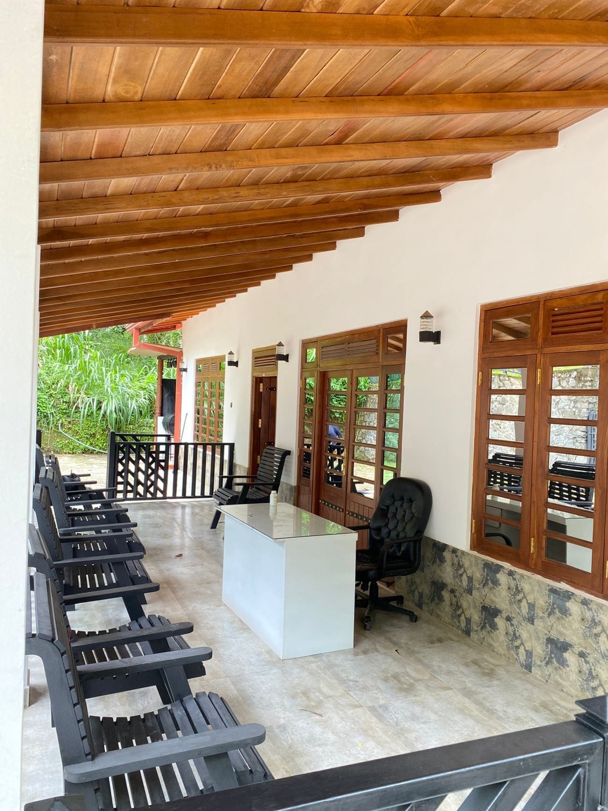 Uma área de estar coberta ao ar livre com um banco comprido, uma mesa pequena e uma cadeira.