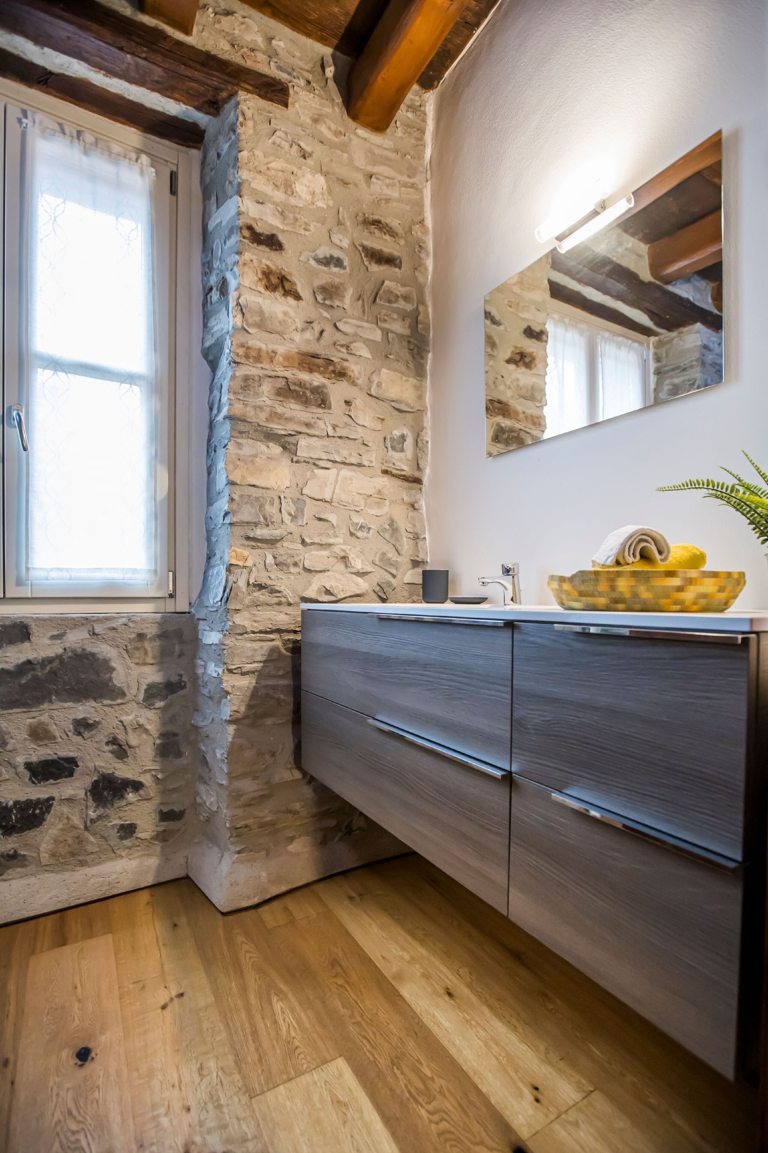 Quarto com parede de pedra, piso de madeira, um espelho, pia e armário de madeira.