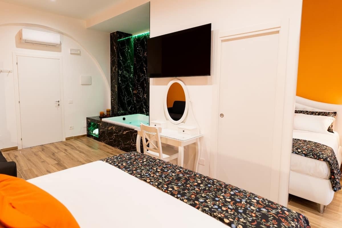 Quarto de hotel moderno com cama, escrivaninha com espelho, televisão e banheiro com parede de mármore.