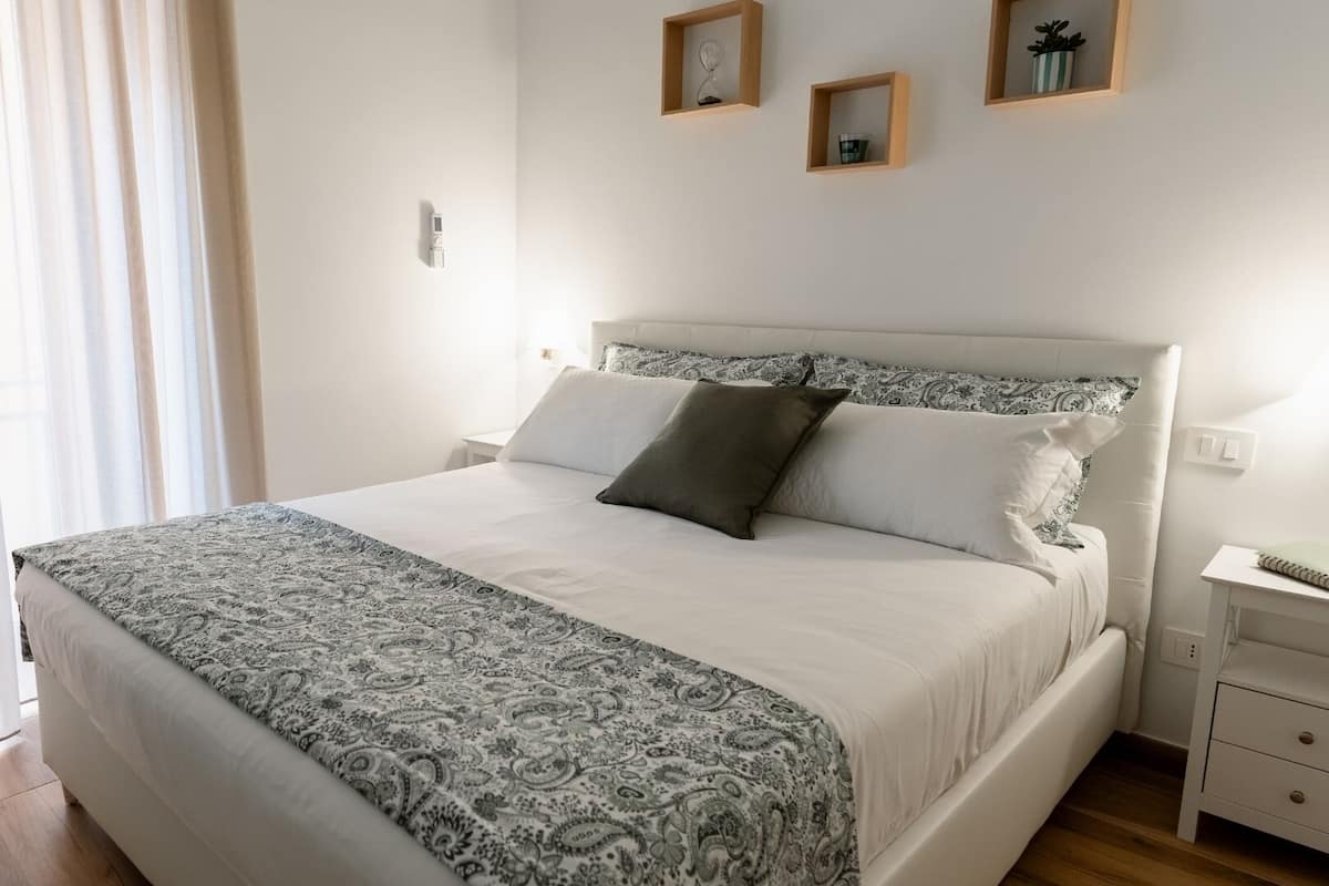 Quarto bem arrumado com cama, mesas de cabeceira e janela com cortinas.