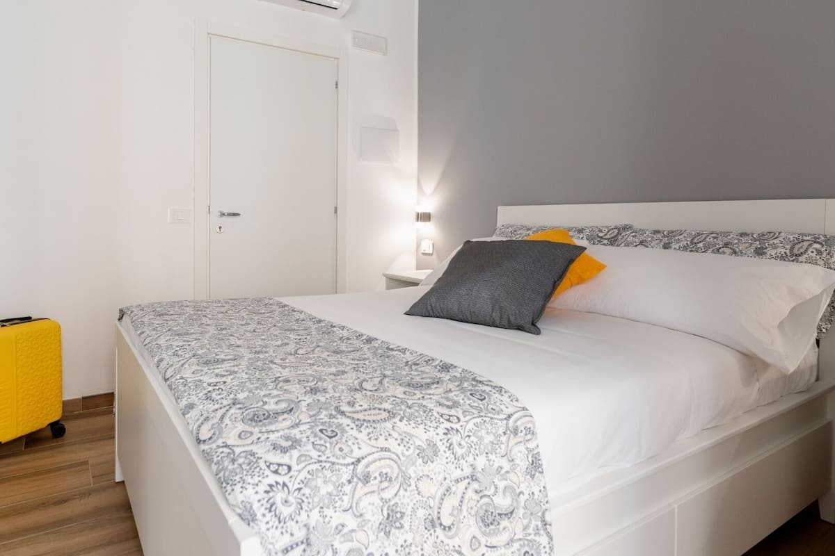Quarto de hotel com uma cama, mala, escrivaninha e porta.