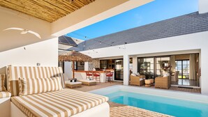 Uma área de piscina moderna ao ar livre, com espreguiçadeira, bar e espaço para refeições.
