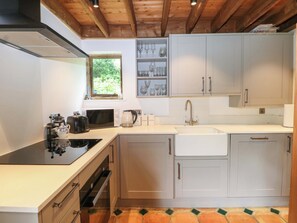 Cozinha compacta com micro-ondas, chaleira e cafeteira. Há uma janela com vista para o verde.