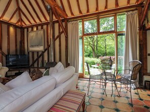 Uma sala de estar aconchegante com sofá, televisão e lareira. Há uma área de jantar com mesa e cadeiras, e grandes janelas com vista para o exterior.