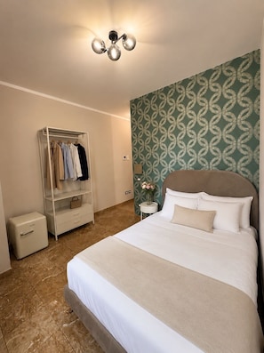 Quarto de hotel com cama, guarda-roupa, uma pequena mesa com um vaso e luminária no teto.