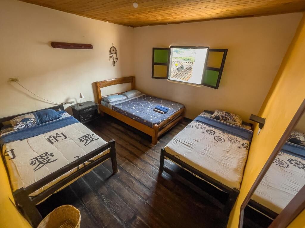 Quarto com duas camas de madeira, uma mesa pequena, prateleira na parede e janela com vista.