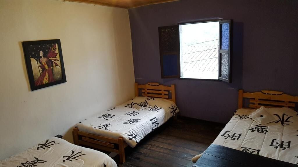 Um quarto com duas camas de madeira, uma janela e um quadro na parede.