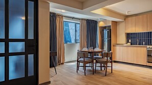 Cozinha moderna com armários de madeira, área de jantar com mesa e cadeiras redondas, e uma janela grande com cortinas.
