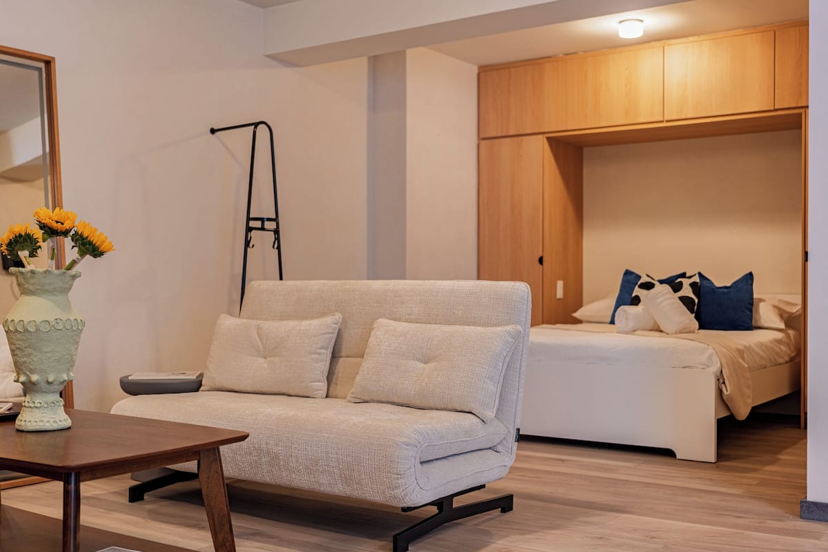 Uma sala moderna com sofá, mesa de centro, cama com almofadas e um armário de madeira.