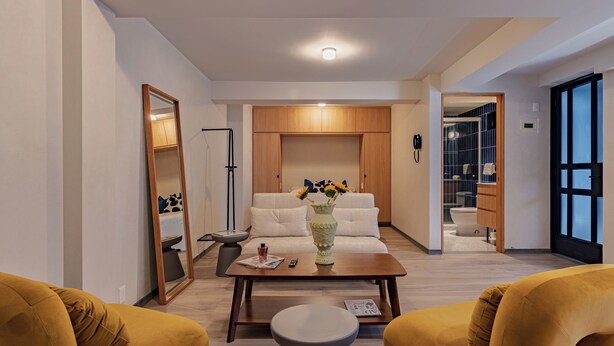Uma sala de estar moderna com um sofá, uma mesa de centro, um espelho e um vaso com flores.