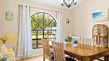 Uma sala de jantar com uma janela grande, um lustre e vista para o exterior.
