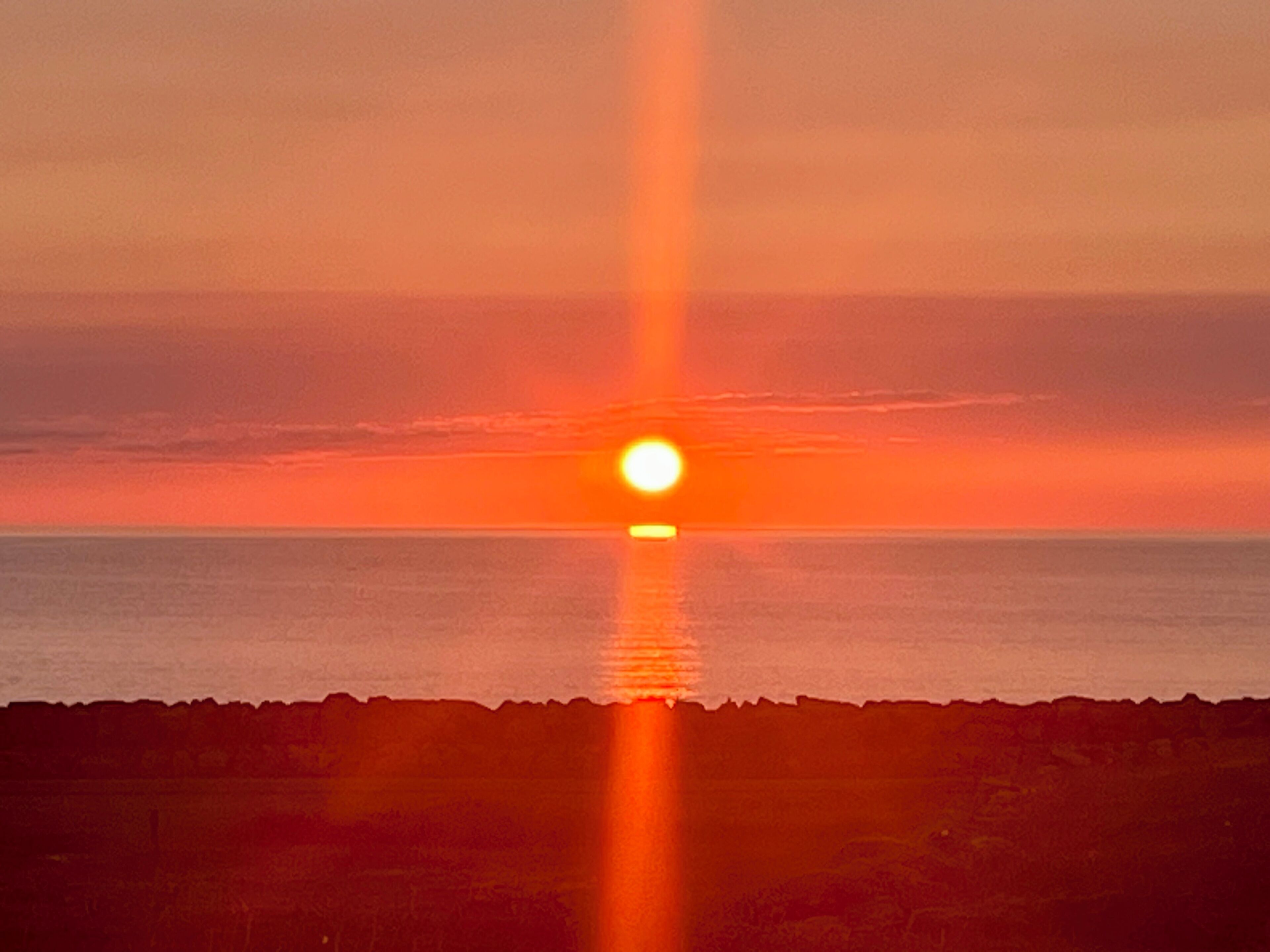 Um pôr do sol sobre a água, com a linha do horizonte visível.