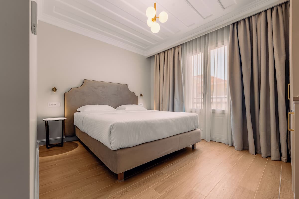 Um quarto com cama, mesa de cabeceira e cortinas.