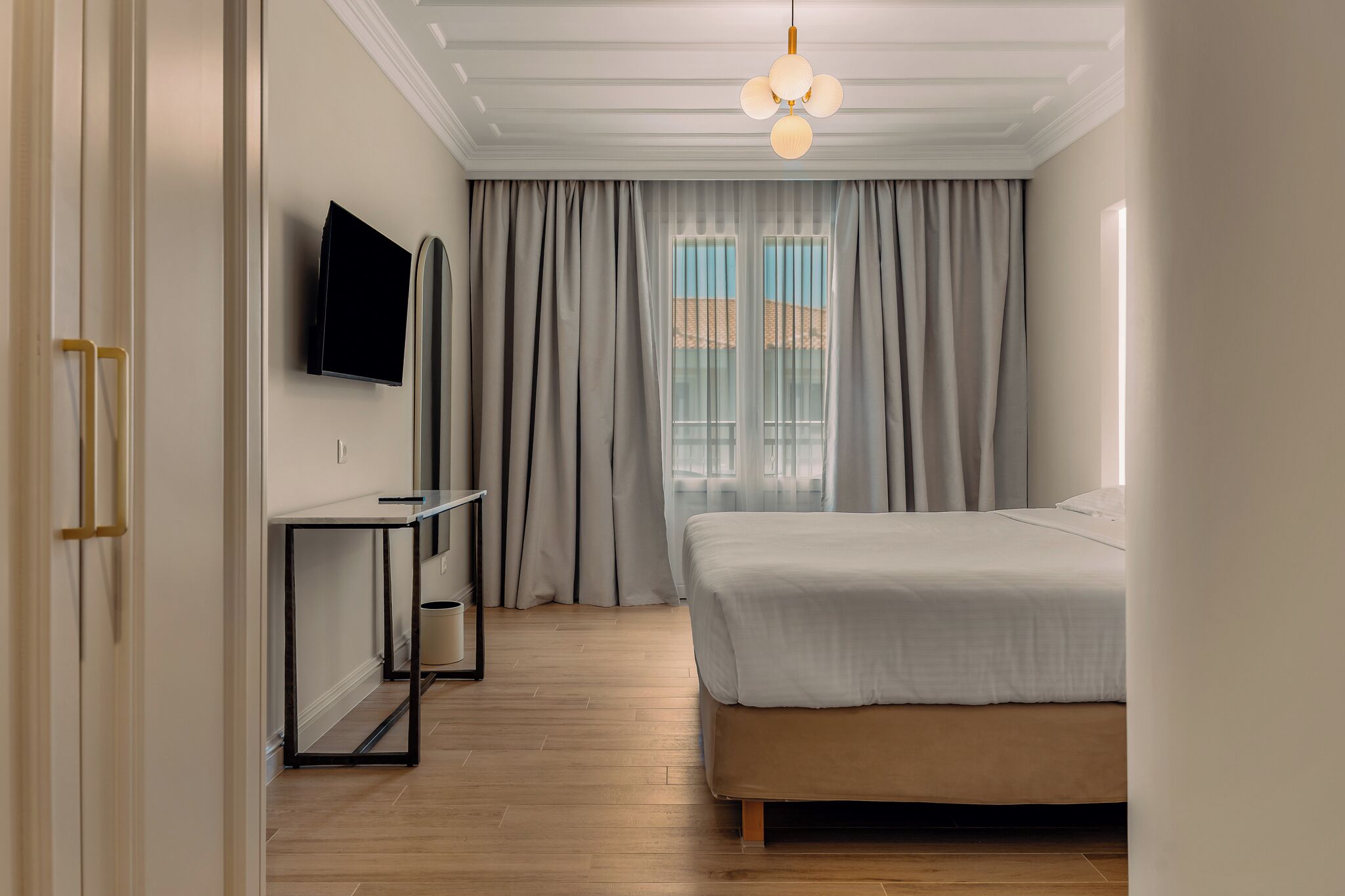 Quarto com cama, televisão, escrivaninha e janela com cortinas.