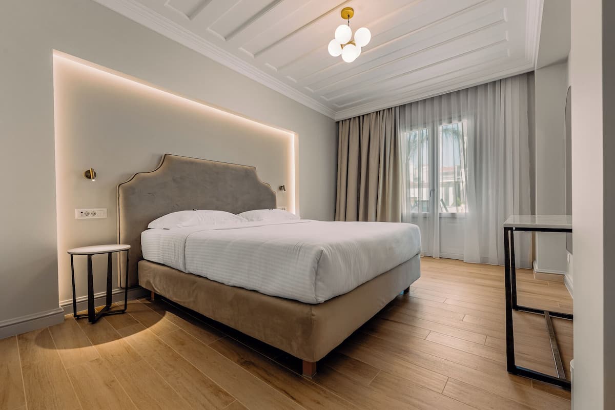 Quarto moderno com cama grande, mesa de cabeceira, luminária de teto e mesa lateral.