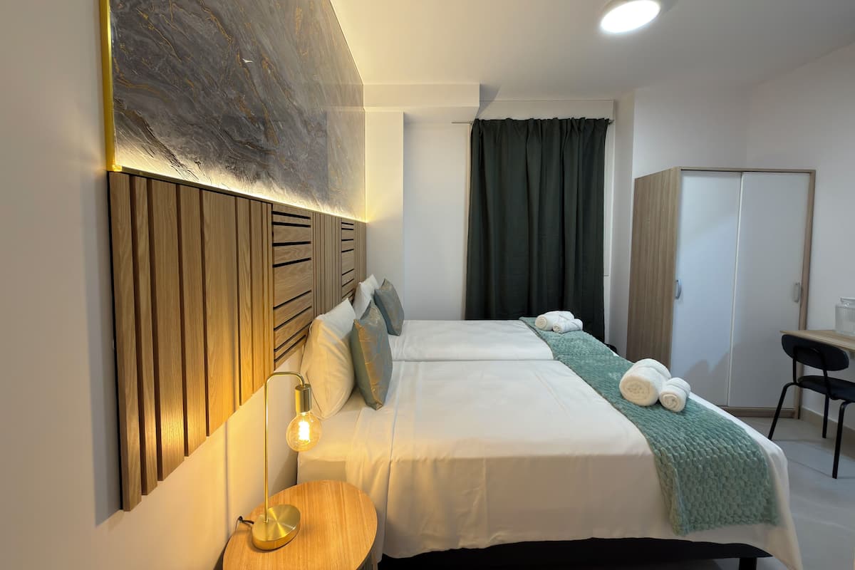 Quarto de hotel com uma cama grande, cabeceira de madeira, abajur, manta verde e um guarda-roupa.