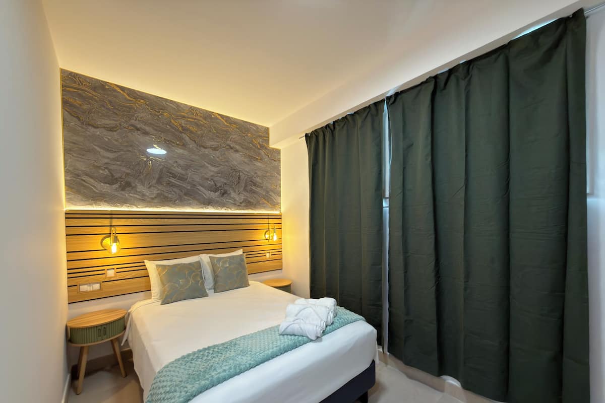 Quarto de hotel moderno com uma cama grande, cabeceira com design semelhante a mármore, mesa de cabeceira pequena e uma janela ampla com cortinas.