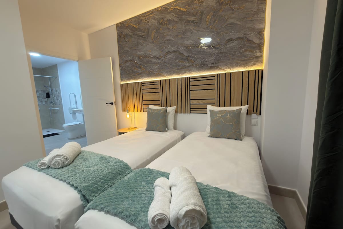 Quarto de hotel com duas camas, banheiro com chuveiro e design de parede semelhante a mármore.