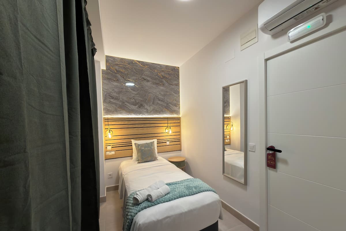 Quarto de hotel moderno com cama, mesa de cabeceira, luminárias fixadas na parede, espelho e aparelho de ar condicionado.