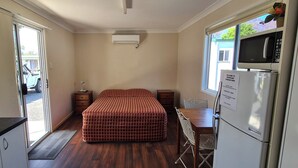 Quarto compacto com uma cama, uma mesinha, micro-ondas e frigorífico.