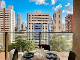 Uma área de refeições com uma mesa posta para dois, com vista para um horizonte urbano repleto de arranha-céus.