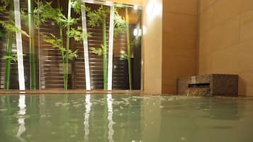 Uma área de spa com uma grande piscina interior, plantas de bambu e um banco de pedra.