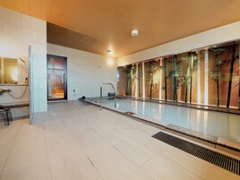 Área de piscina interna limpa com parede de vidro transparente, um banco e área de chuveiro.