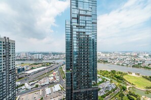 Um edifício alto com fachada de vidro, rodeado por uma paisagem urbana e um rio.