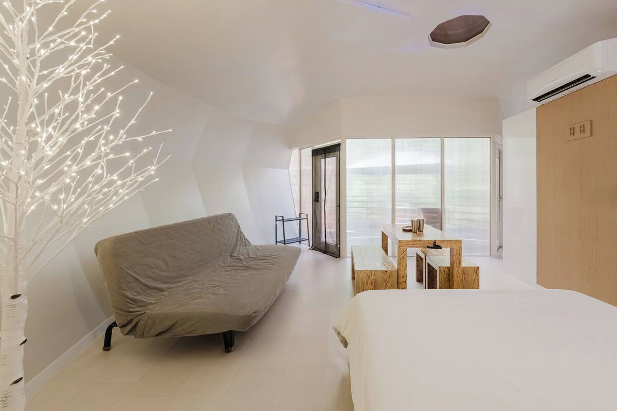 Quarto de hotel moderno com cama, sofá, escrivaninha e uma janela grande.