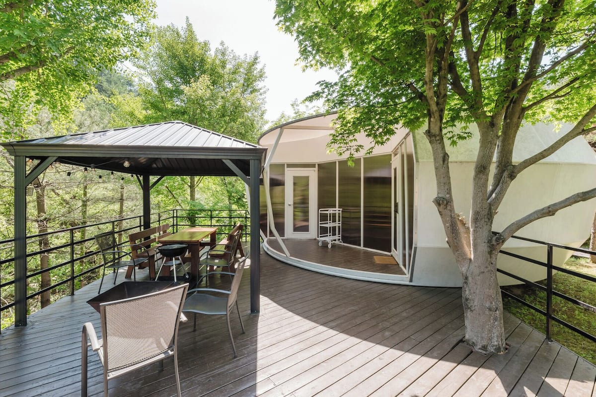 Um deck de madeira com móveis de exterior, uma área de estar coberta e uma sala envidraçada.