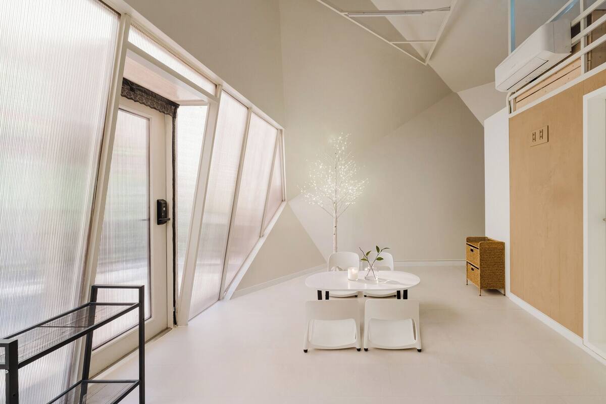 Quarto de hotel moderno com uma mesa redonda, cadeiras, uma pequena planta e um guarda-roupa.